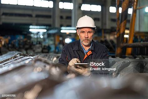흰색 안전모와 안전 장갑을 착용하고 대형 작업장에서 중장비에 디지털 태블릿을 사용하여 작업하는 수석 남성 엔지니어 55 59세에
