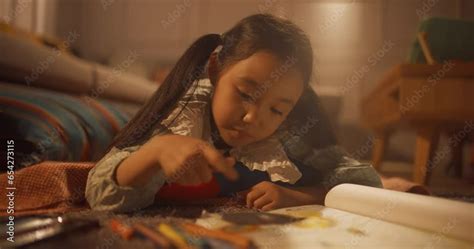 따뜻한 조명이 비치는 거실 바닥에 누워 그림을 색칠하는 소녀의 영상 시네마틱 샷 Видео Stock Adobe Stock