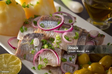 붉은 양파 발효 오이 감자 올리브 레몬을 곁들인 절인 청어 슬라이스를 어두운 나무 테이블에 흰색 접시에 담았습니다 감자 요리에