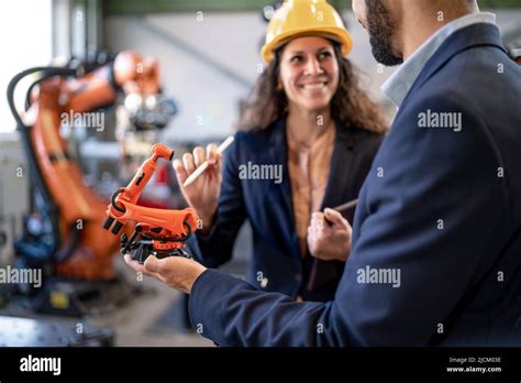 Man Engineer Holding Model Of Industrial Robotic Arm And Showing To Collegue In Factory Stock
