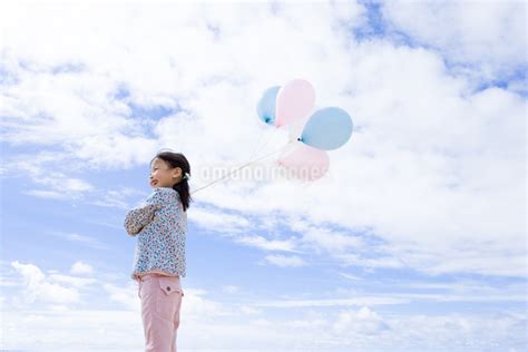 青空と風船を持っている女の子の写真素材 FYI ストックフォトのamanaimages PLUS