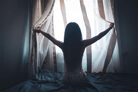 Premium Photo The Girl Sits On The Bed And Opens The Curtains