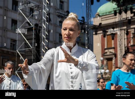 A Serene Tai Chi Master In A Flowing White Suit Gracefully Performs On A Bustling Street Her