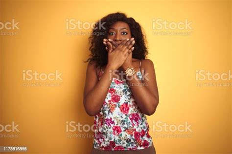 고립 된 노란색 배경 위에 꽃 여름 티셔츠를 입고 아프리카 계 미국인 여성은 실수로 손으로 입을 덮는 충격을 받았습니다 비밀 개념입니다 T 셔츠에 대한 스톡 사진 및 기타