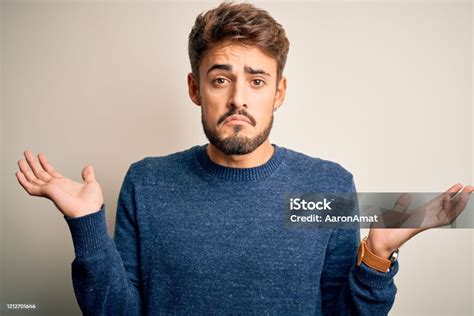 흰색 배경에 서 캐주얼 스웨터를 입고 수염을 가진 젊은 잘 생긴 남자는 팔과 손을 들고 단서와 혼란 스러운 표정 의심 개념 감정에 대한 스톡 사진 및 기타 이미지 Istock