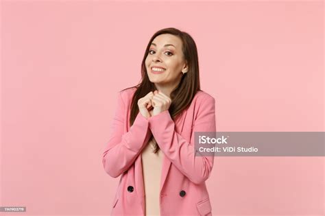 재킷에 예쁜 웃는 매력적인 젊은 여자의 초상화는 스튜디오에서 파스텔 분홍색 벽 배경에 고립 된 얼굴 근처의 주먹을 쥔 다