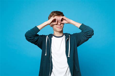 눈 근처에 손을 잡고 파란 벽 배경에 고립 된 안경이 나 쌍안경을 모방 하는 우연한 옷에 쾌활 한 재미 있는 젊은 남자 사람들은 진심으로 감정 라이프 스타일 개념입니다 복사