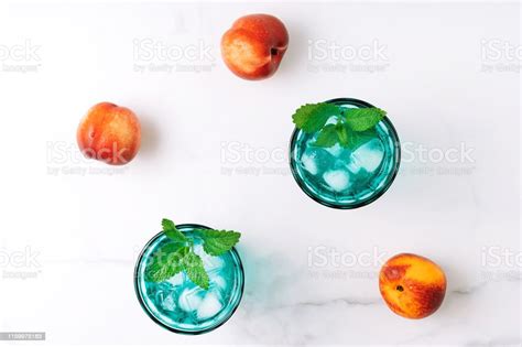 차가운 음료와 얼음 조각이있는 아름다운 빈티지 청록색 안경 2 개와 신선한 녹색 민트 잎과 흰색 대리석 테이블에 3 개의 넥타린이 장식되어 있습니다 0명에 대한 스톡 사진