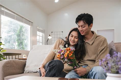 Romantic Young Asian Couple Embracing With Holding Flowers And Smiling