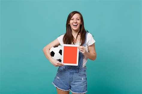 축구 공 파란색 청록색 배경에 고립 된 빈 빈 화면 태블릿 Pc 컴퓨터를 들고 웃는 여자 축구 팬 사람들의 감정 스포츠 가족 레저 개념입니다 복사 공간을 모의 합니다 갈색