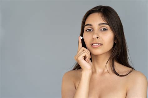 젊은 매력적인 여자 소녀는 회색 스튜디오 배경 얼굴 화장품 스파 스킨 케어 개념 자연 미용 광고 복사 공간 초상화에 고립 된 카메라에서 얼굴 표정에 크림을 적용 가꿔주기에