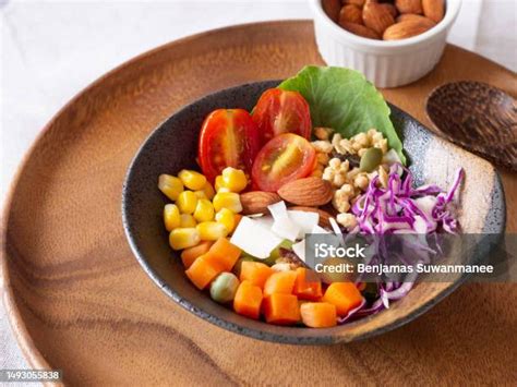 토마토 옥수수 당근 완두콩 붉은 양배추 양상추 그래놀라 바삭한 코코넛 칩을 보른 그릇에 얹고 나무 접시 위에 아몬드를 얹은 야채 샐러드 0명에 대한 스톡 사진 및 기타