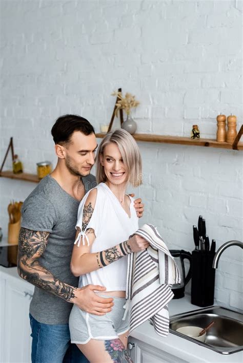 Side View Of Tattooed Man Hugging Smiling Girlfriend With Towel Stock