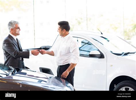 Senior Car Salesman Handing Over New Car Key To Customer At Showroom