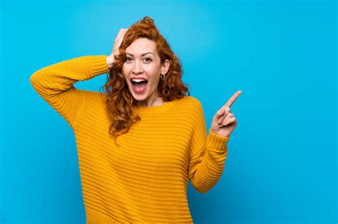 빨간 머리 여자 와 노란색 스웨터 놀랐다 고 가리키는 손가락 에 그 측면 가리키기에 대한 스톡 사진 및 기타 이미지 가리키기