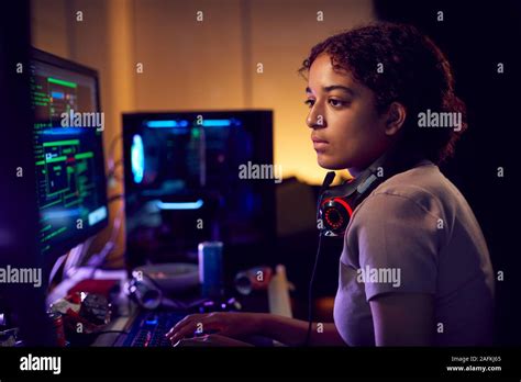 Female Teenage Hacker Sitting In Front Of Computer Screens Bypassing Cyber Security Stock Photo