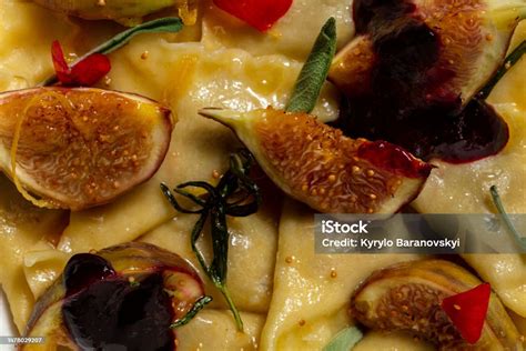 오리 필레 만두에 무화과 체리 소스 식용 보라색 꽃잎 로즈마리 체리 소스를 얹었습니다 음식은 타원형의 흰색 세라믹 접시에 놓여 있습니다 접시는 어두운 패브릭 배경 커피