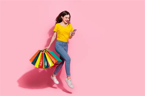 가방을 들고 달리는 멋진 밀레니엄 세대 갈색 머리 숙녀의 전체 길이 사진 핑크 배경에 고립 된 티셔츠 청바지 신발을 착용하십시오 쇼핑백에 대한 스톡 사진 및 기타 이미지