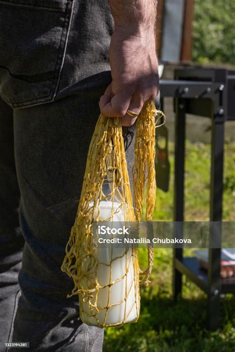 한 남자가 재사용 가능한 에코 스트링 메쉬 쇼핑백에 우유 한 병을 들고 다닙습니다 쇼핑 복고풍 스타일 친환경 플라스틱 프리 컨셉을 위한 현대적인 재사용 가능한 가방 0에