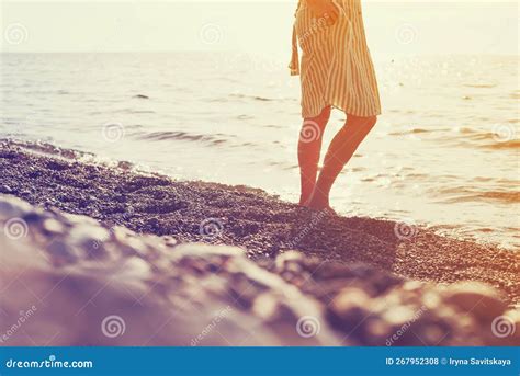 Girl In A Dress With Bare Feet Walks Along A Pebble Beach Along The Sea