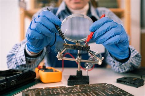 engineer testing microcircuit through magnifier using multimeter