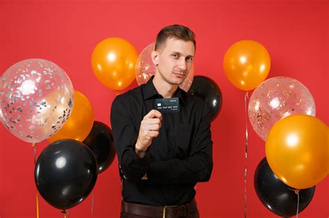 밝은 빨간색 배경에 공기 풍선에 신용 카드를 들고 검은 클래식 셔츠에 잘생긴 젊은 남자 세인트 발렌타인 국제 여성의 날 해피