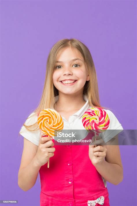 막대기 또는 롤리팝에 큰 사탕을 먹는 소녀 달콤한 어린 시절 개념 웃는 얼굴에 소녀는 손에 두 개의 거대한 다채로운 롤리팝 보라색 배경을 보유하고 있습니다 긴 머리를 가진