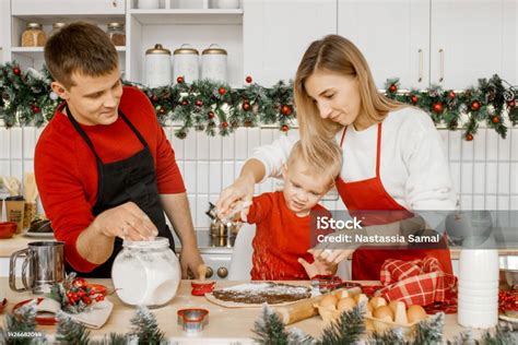 부엌에서 크리스마스 쿠키를 요리하는 행복한 가족 젊은 미소 짓는 어머니는 어린 아들이 반죽에 밀가루를 뿌리도록 도와줍니다 부모와 함께 요리하는 아이들 작은 요리사 함께