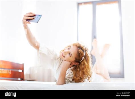 Casual careless girl at home using smart phone. Lying in bed scrolling ...