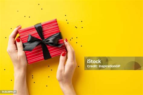 블랙 프라이데이 개념 고립된 노란색 배경에 검은 색종이 위에 리본 리본 활이 있는 빨간 선물 상자를 들고 있는 여자의 손의 1인칭 평면도 사진 11월에 대한 스톡 사진 및