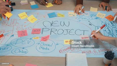 나무 테이블 Sactr의 큰 계획 시트를 중심으로 협업하는 다채로운 스티커 메모와 손으로 새 프로젝트를 개발하기 위한 창의적인 브레인스토밍 세션 가계에 대한 스톡 사진 및