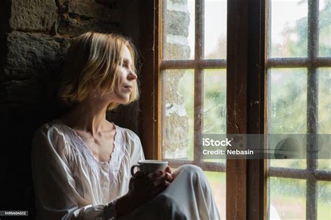 생각에 잠긴 표정을 한 여자가 창가에서 커피를 마신다 흰 셔츠를 입은 중년 여성 슬픈 표정 생각 여자에 대한 스톡 사진 및 기타 이미지 Istock