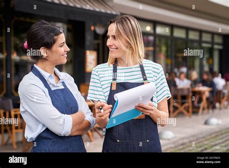Mid Shot Of Two Female Restaurant Owners Checking A List Outside Their Restaurant Stock Photo