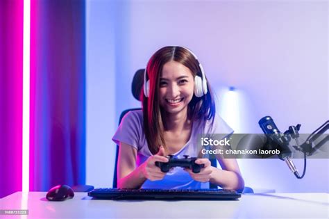 프로 게이머 거실에 컴퓨터 Pc가있는 의자에 앉아있는 젊은 아시아 예쁜 여자 행복한 여성 전문 스트리머 중국어 착용 헤드폰
