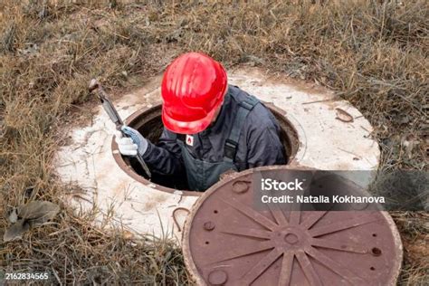 헬멧을 쓴 작업자가 조정 가능한 렌치를 사용하여 우물에 앉아 있습니다 급수 장치의 유지 보수 및 수리 50 54세에 대한 스톡