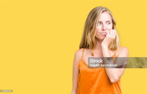 격리 된 배경 찾고 스트레스와 긴장에 오렌지색 셔츠를 입고 아름 다운 젊은 여 자가 손톱을 물어 뜯고 입에 손 불안 문제입니다 T 셔츠에 대한 스톡 사진 및 기타 이미지