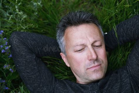 Portrait Of Middle Aged Man Lying On Field Among Blue Flowers And Green