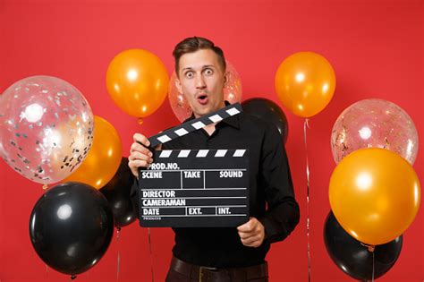 밝은 빨간색 배경에 공기 풍선에 Clapperboard 만드는 고전적인 흑인 영화를 들고 검은 셔츠에 있는 젊은이 깜짝 놀라게 한다 국제 여성의 날 해피 뉴가 어 생일 이랑
