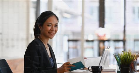 노트북을 들고 사무실 책상에 앉아 카메라를 향해 웃고 있는 자신감 넘치는 사업가 사진 Unsplash의 태국 이미지