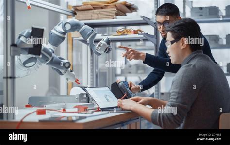 Black Male Engineer Shares His Ideas With Asian Developer While Controlling Robotic Arm During