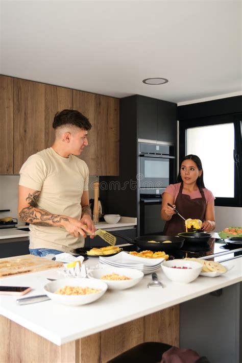 Two Young Latin People Talking While Cooking Arepas And Llapingachos