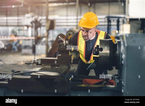 Young Engineer Male Worker Work In Heavy Metal Industry Cnc Lathe Machine With Safety Stock