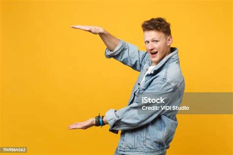 쾌활 한 젊은 남자에 데님 캐주얼 옷 몸짓은 노란색 주황색 배경에 고립 된 수직 작업 공간을 보여주는 크기 사람들은 진심으로 감정 라이프 스타일 개념입니다 복사 공간을 모의