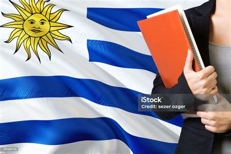 우루과이 언어 개념 학습 백그라운드에서 우루과이 국기와 함께 서 있는 젊은 여자 책을 들고 교사 오렌지 빈 책 표지 교사 교육