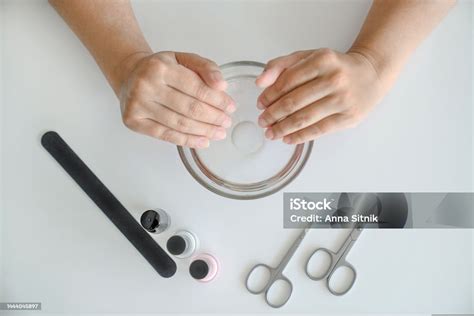 여자의 손은 유용한 물질이 든 따뜻한 물로 목욕을하고 있습니다 네일 파일 가위 및 바니시 병이 테이블 옆 평면도에 있습니다