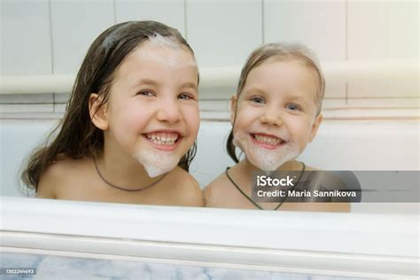 거품에 두 아름다운 어린 소녀는 화장실에 앉아있는 동안 재미를 가지고있다 머리와 얼굴에 거품이 있는 장난기 넘치는 아이들 어린이