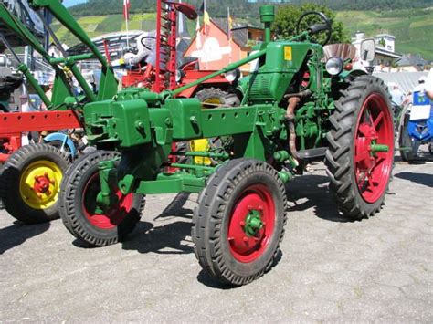 an old green tractor with red wheels parked in a parking lot next to