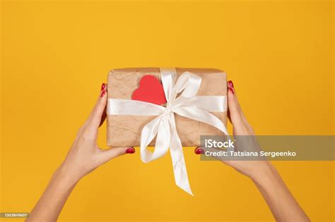 리본과 인공 하트로 감싸인 선물 상자를 들고 있는 여성의 손 노란 배경에 빨간 손톱으로 부드러운 여성의 손 2월에 대한 스톡 사진 및 기타 이미지 Istock
