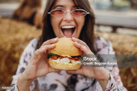 길거리 음식 축제 길거리 음식 축제에서 맛 있는 비 건 버거를 먹는 선글라스의 세련 된 소식통 소녀 여름 거리에서 야채와 함께 행복 한 보헤미안 여자 시음과 물고 햄버거