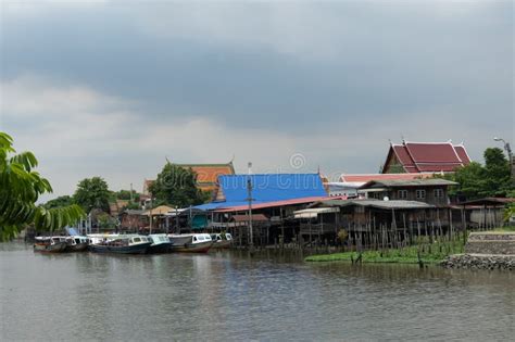 A Traditional Old House By The River With Boats Passing By On